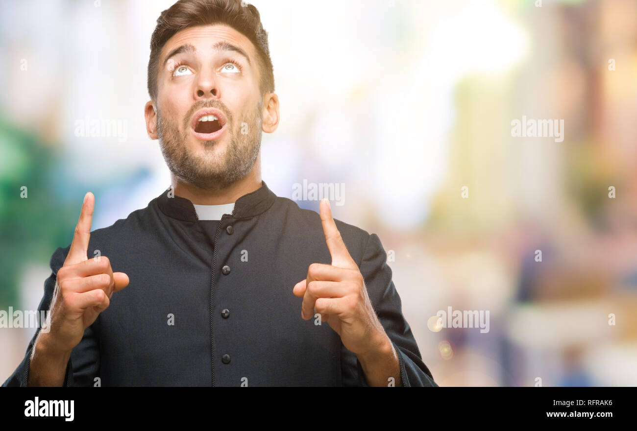 Young catholic christian priest man over isolated background amazed and ...