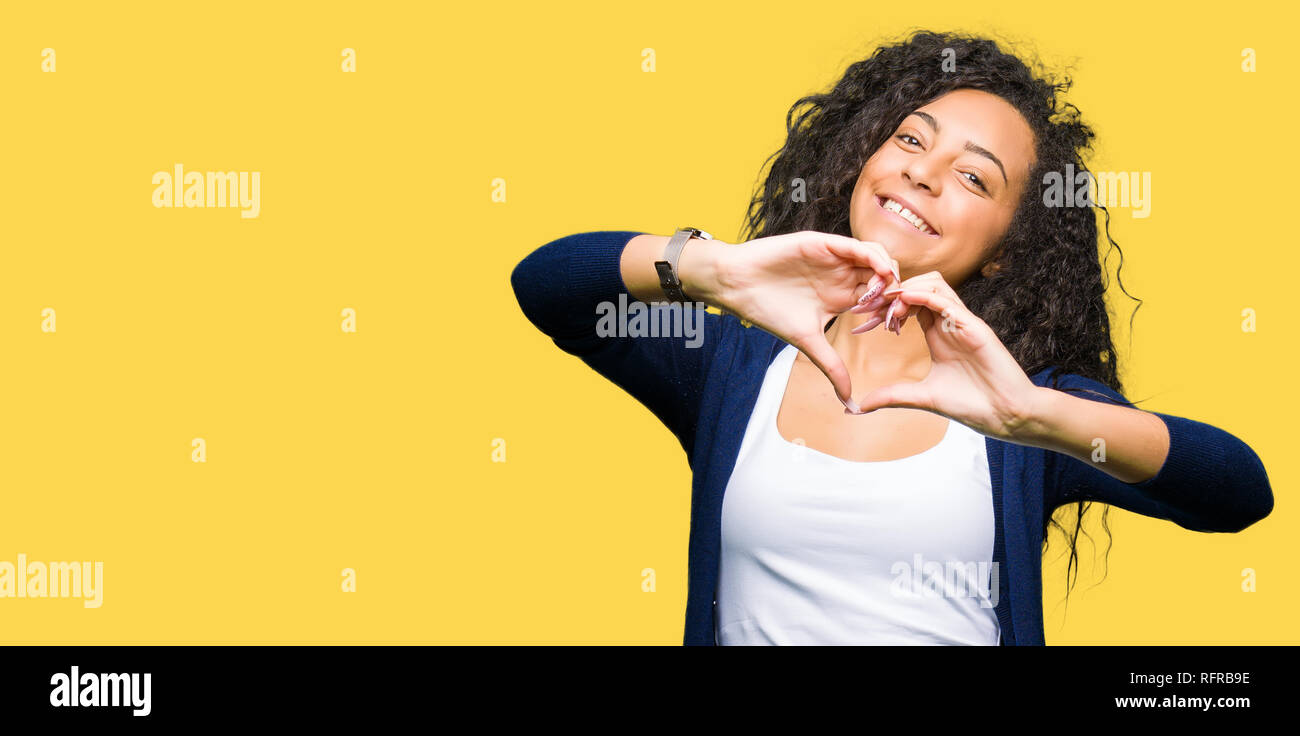 Young beautiful girl with curly hair smiling in love showing heart ...