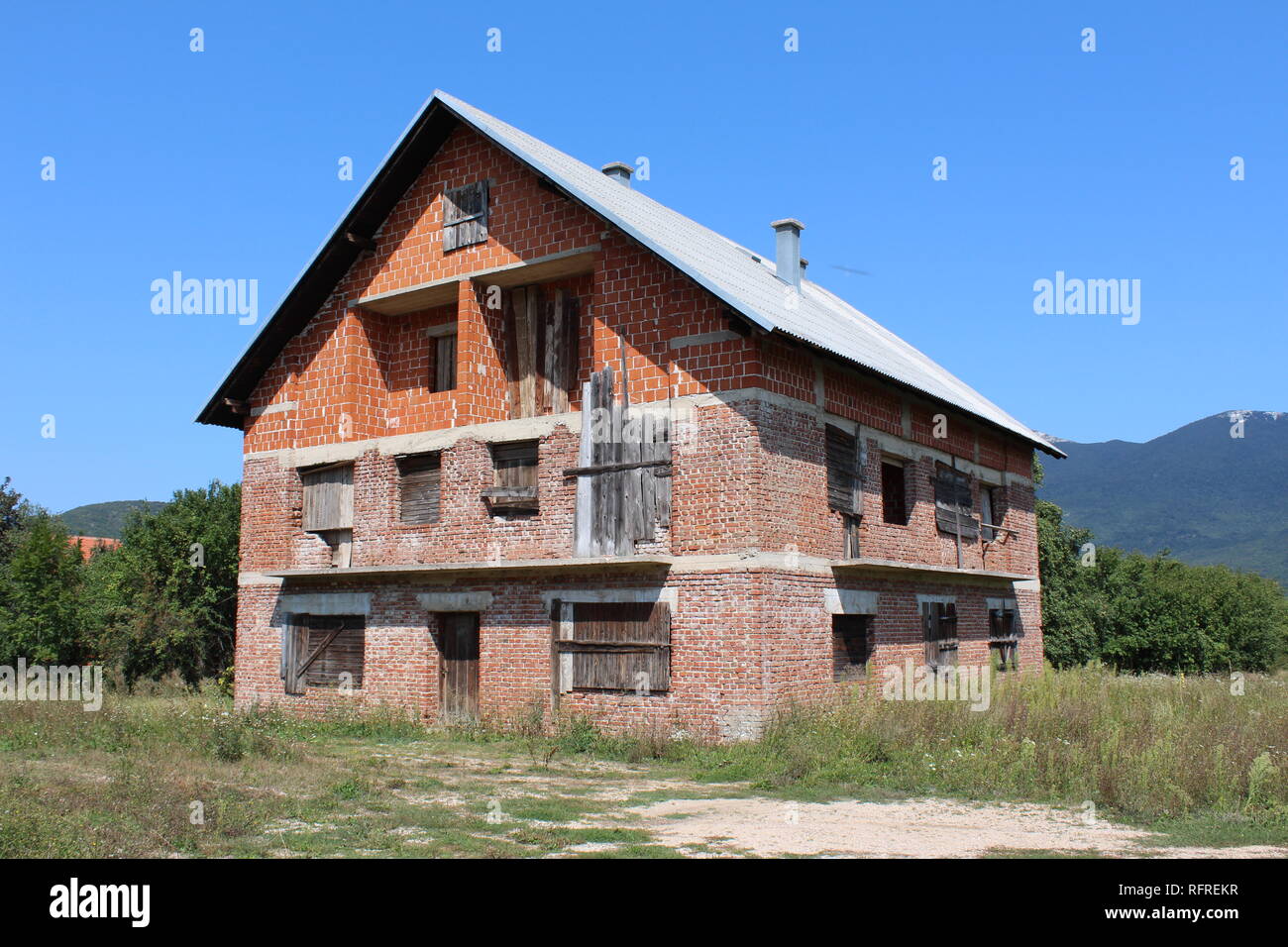 Unfinished abandoned red brick suburban house with boarded windows and ...