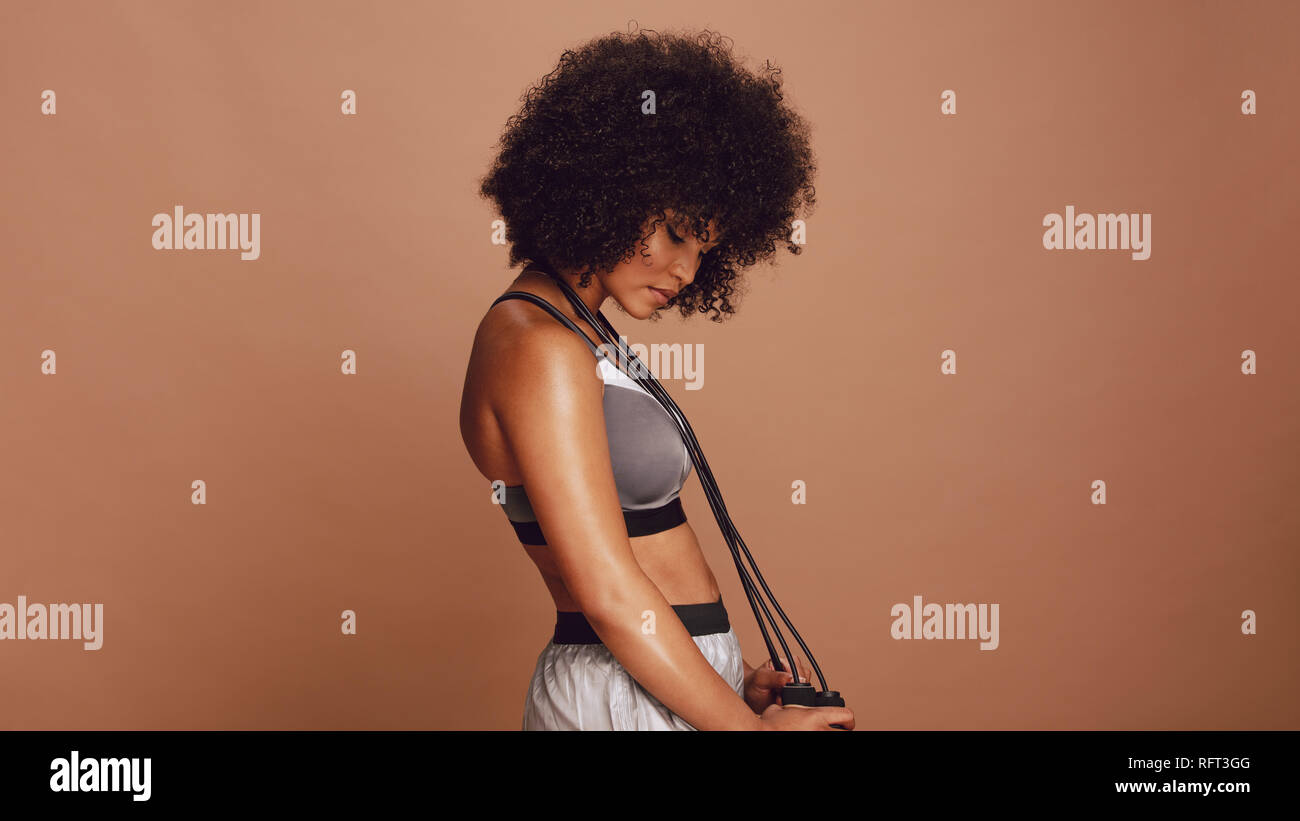 Side view of fitness woman with a jump rope standing against brown ...