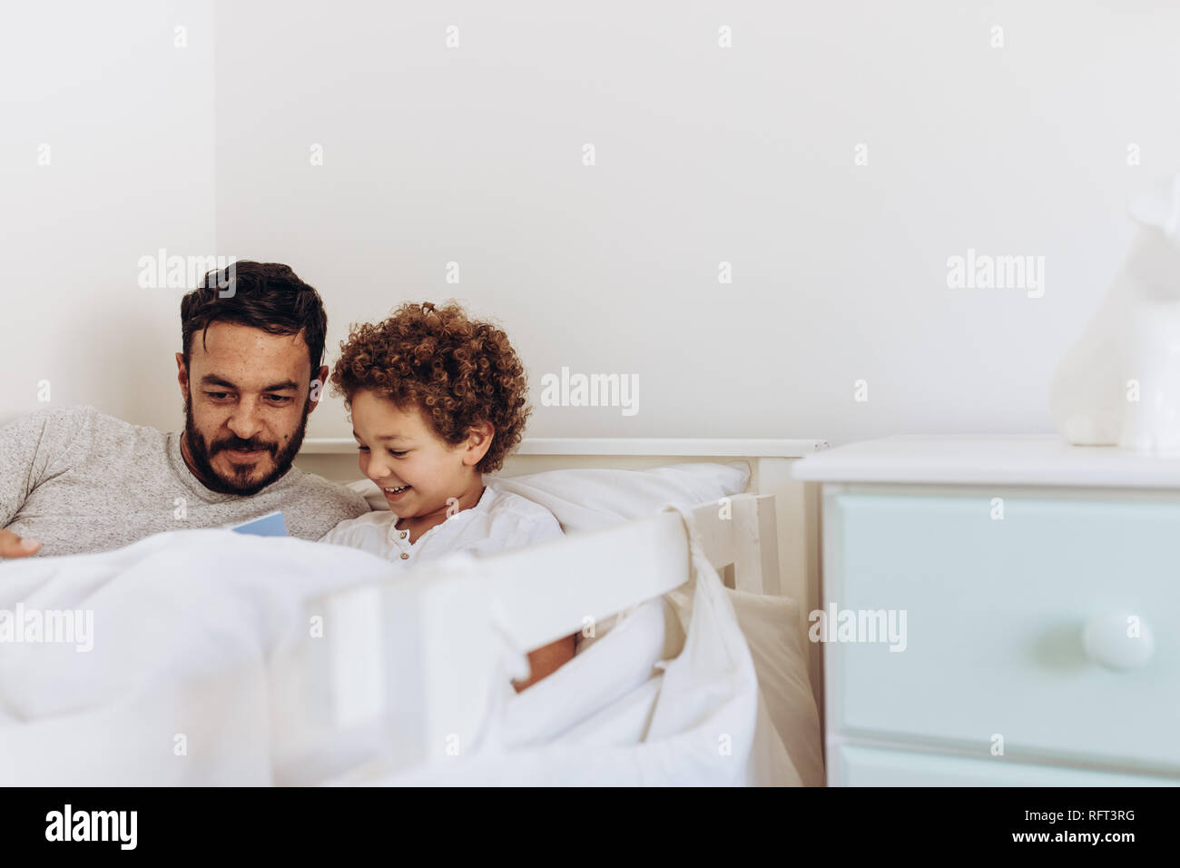 Boy reading a story sitting on bed with his father beside him. Father ...