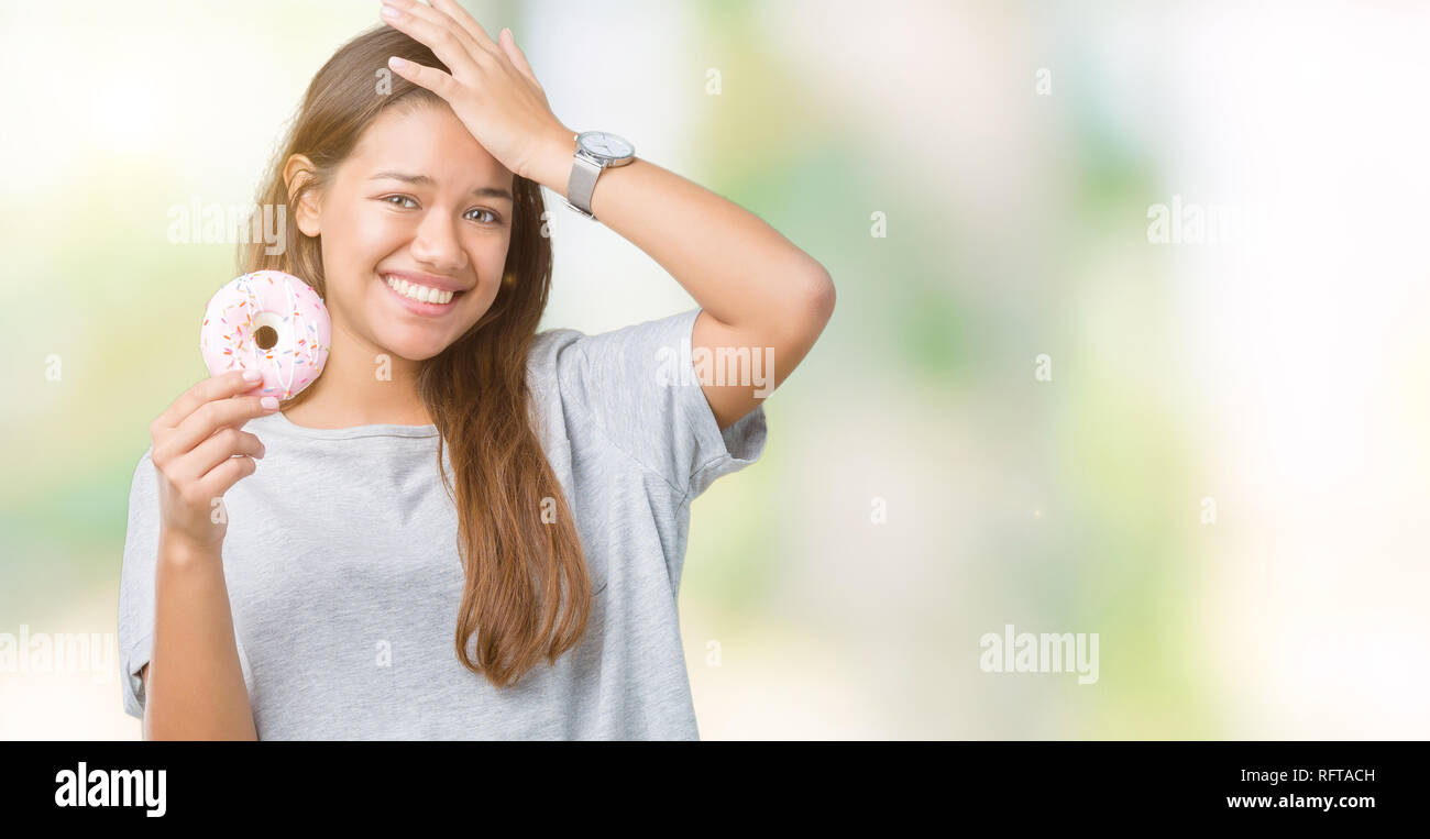 Young beautiful woman eating pink donut over isolated background ...