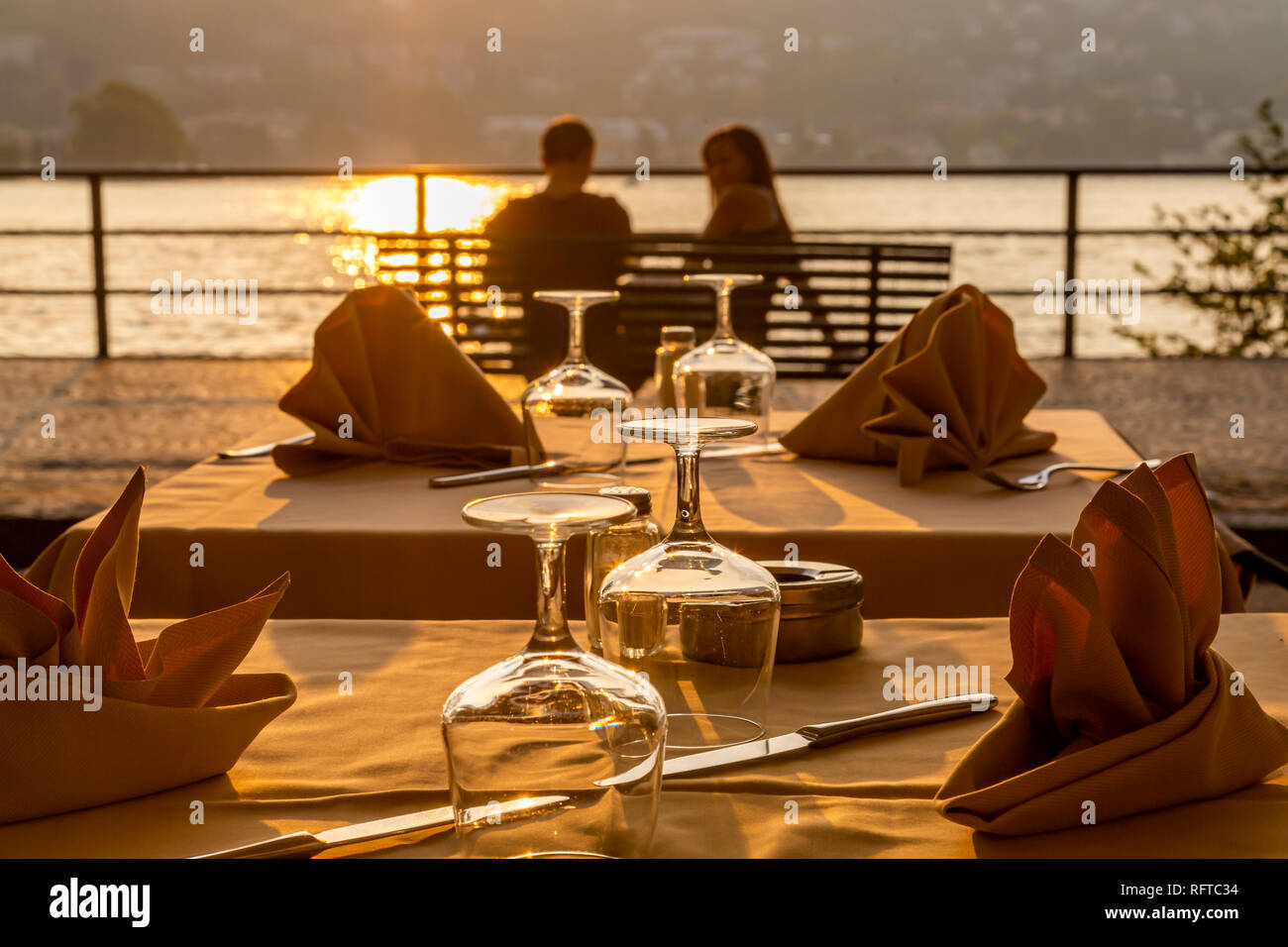 Restaurant tables set for dinner and couple overlooking lake at sunset ...