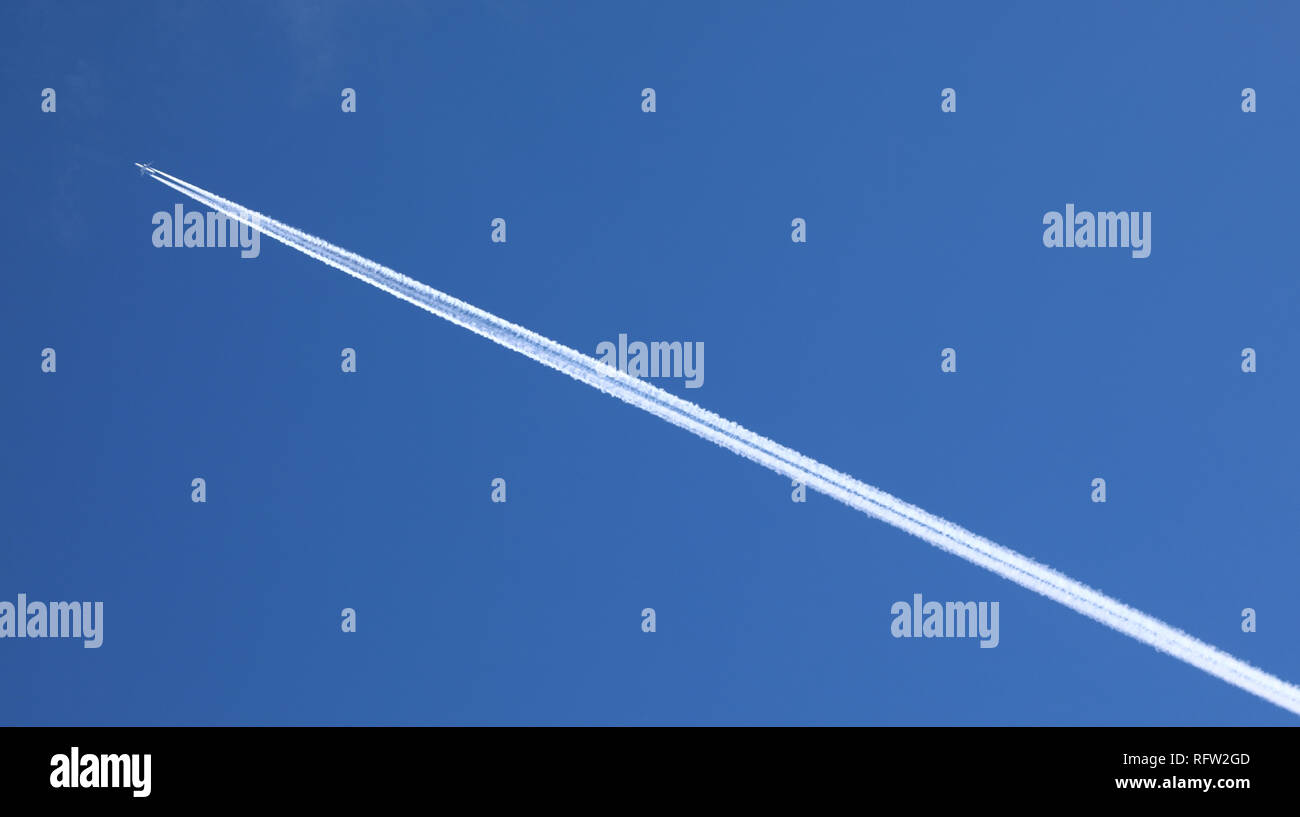 Engine exhaust contrails forming behind an aircraft in the blue sky ...