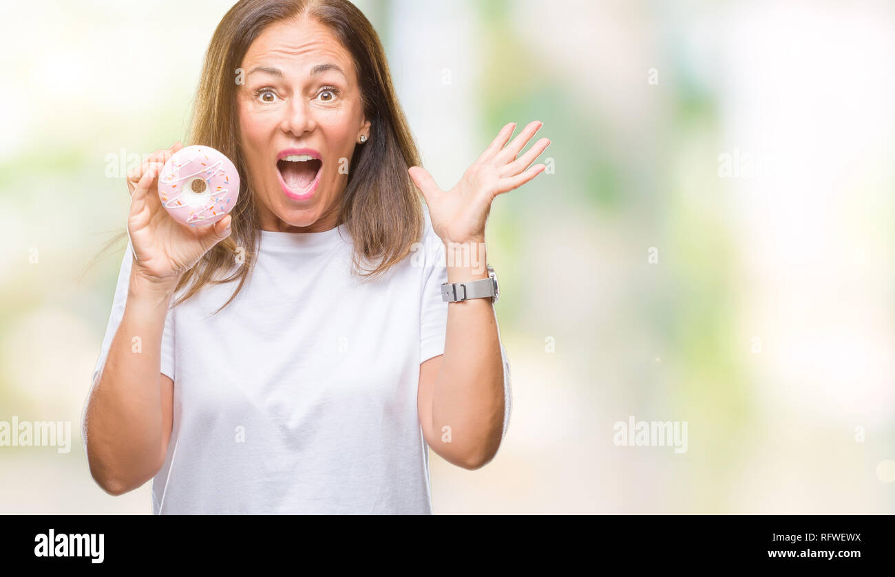 Middle age hispanic woman eating pink donut over isolated background ...