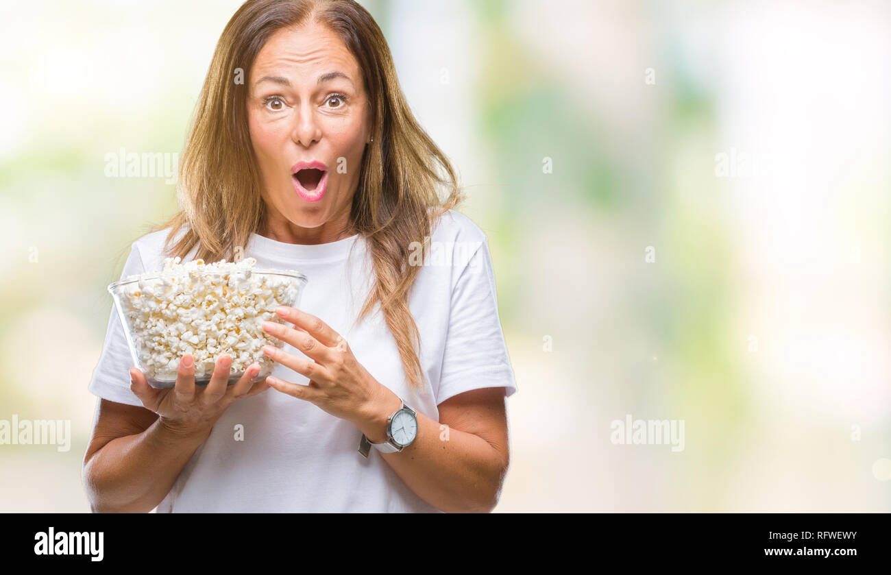 Middle age hispanic woman eating popcorn over isolated background ...