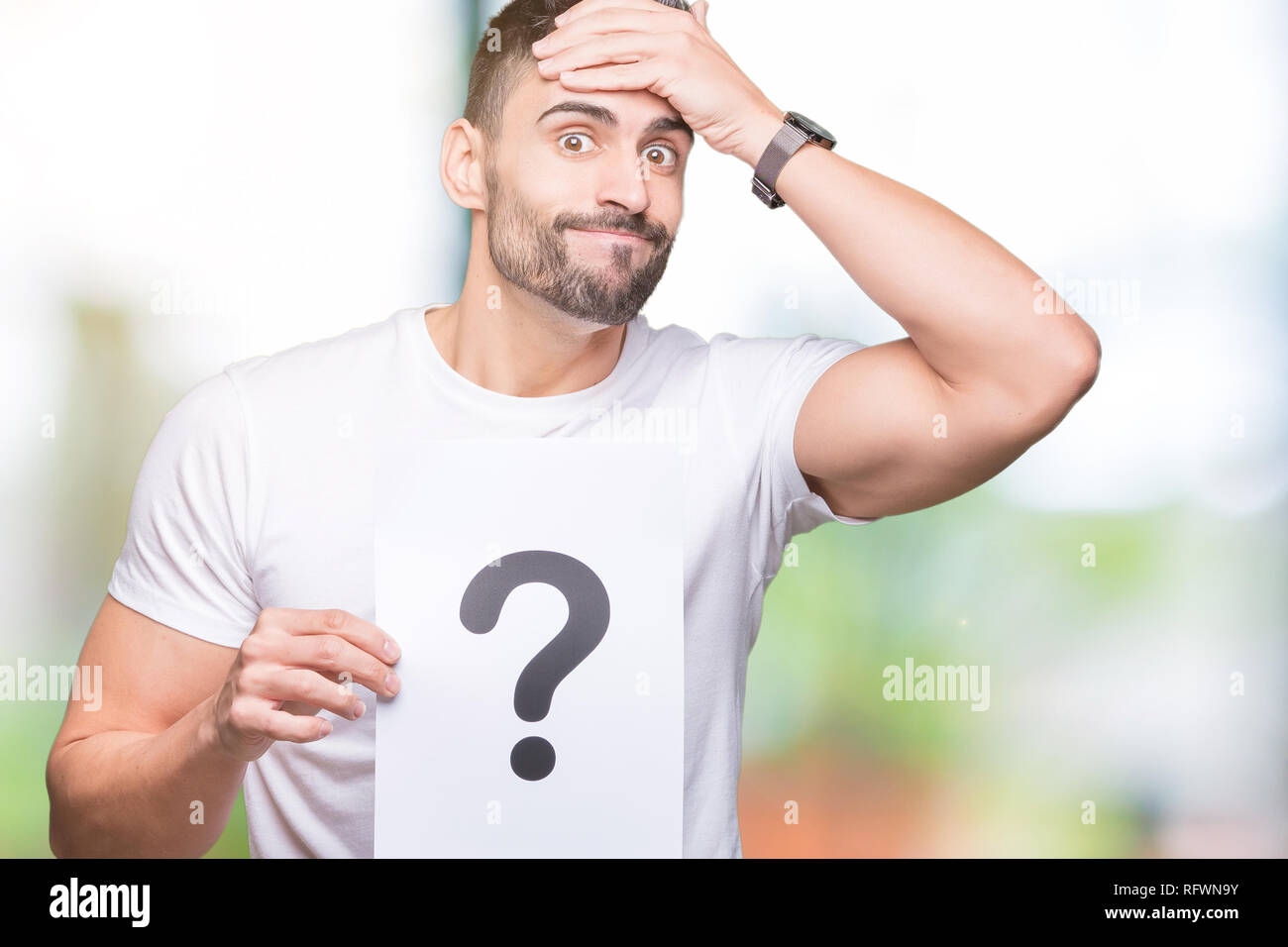 Handsome young man holding paper with question mark over isolated ...