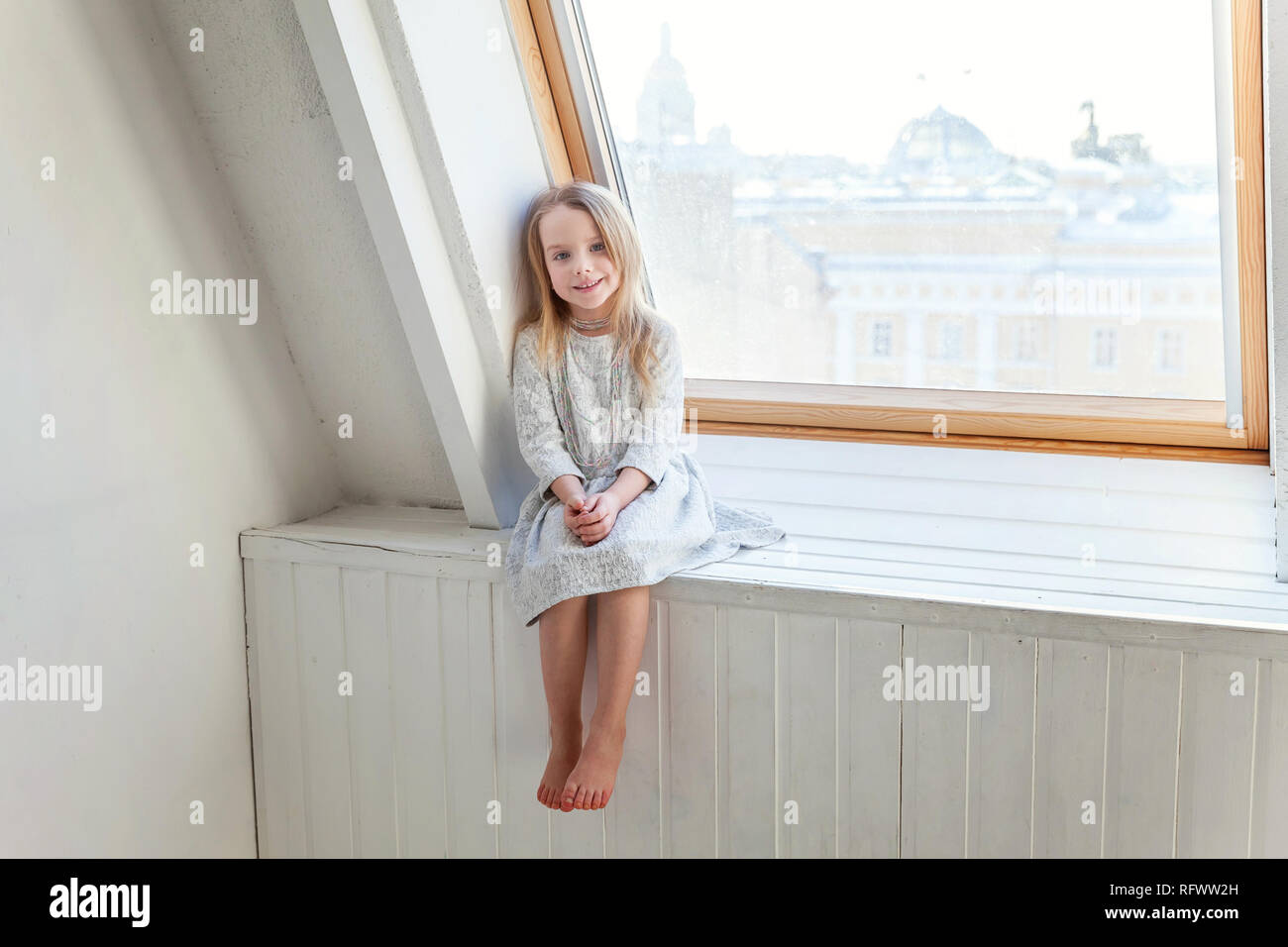 Little cute sweet smiling girl in white dress sitting on the window ...