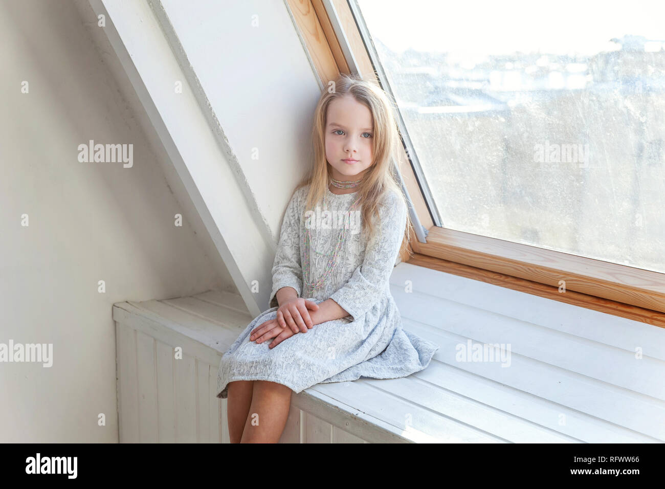 Little cute sweet smiling girl in white dress sitting on the window ...