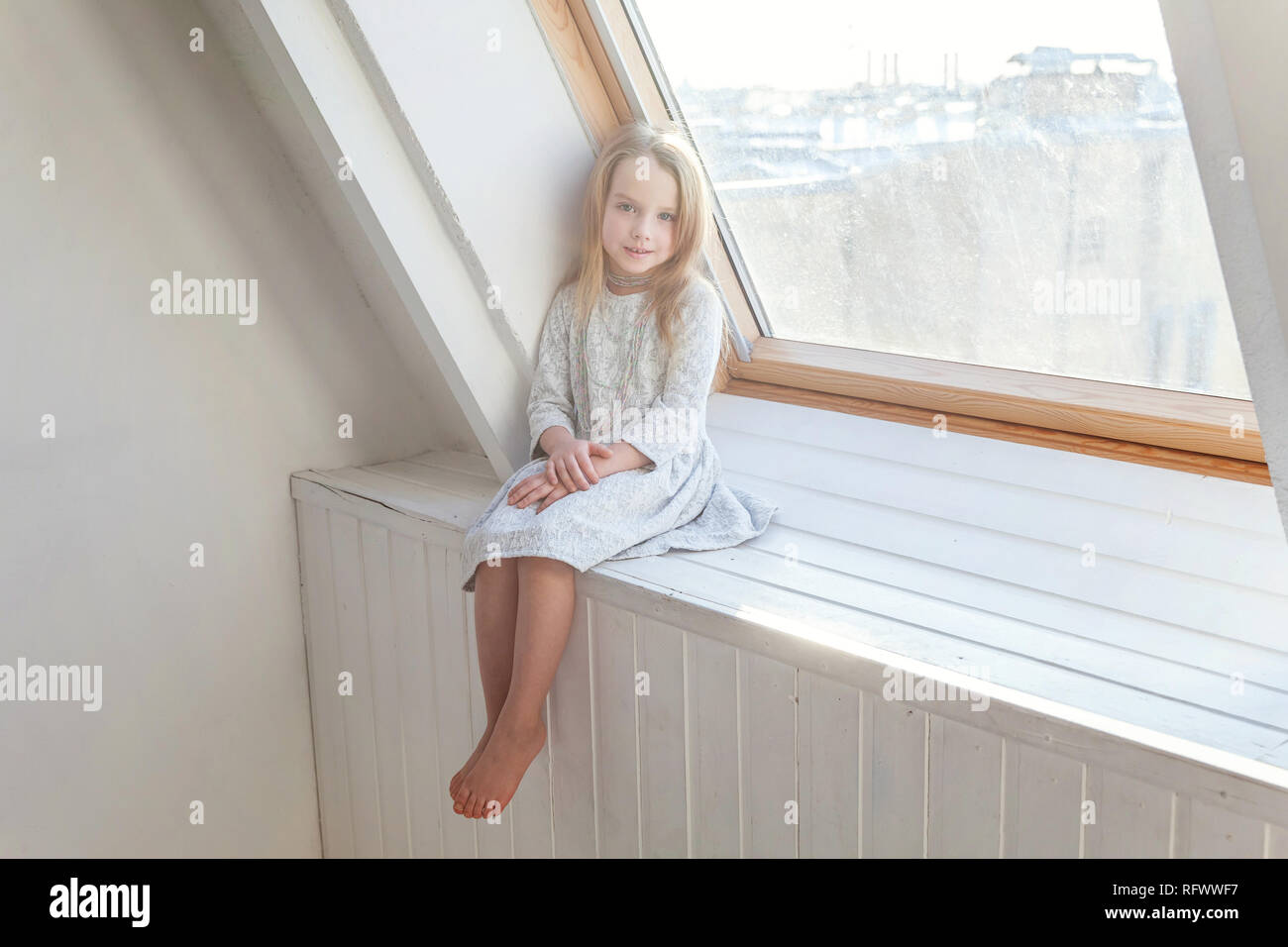 Little cute sweet smiling girl in white dress sitting on the window ...