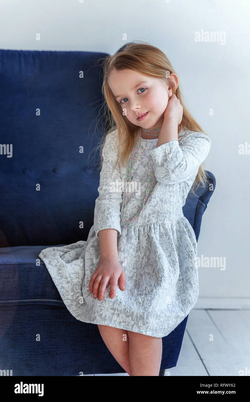 Sweet little girl in grey dress at home sitting on modern cozy blue ...