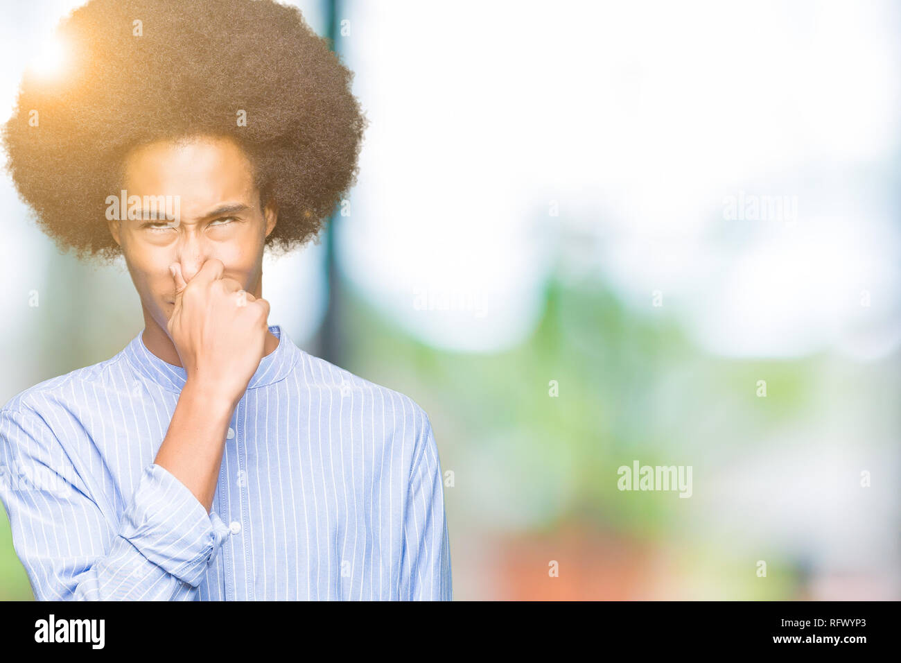 Young african american man with afro hair smelling something stinky and ...