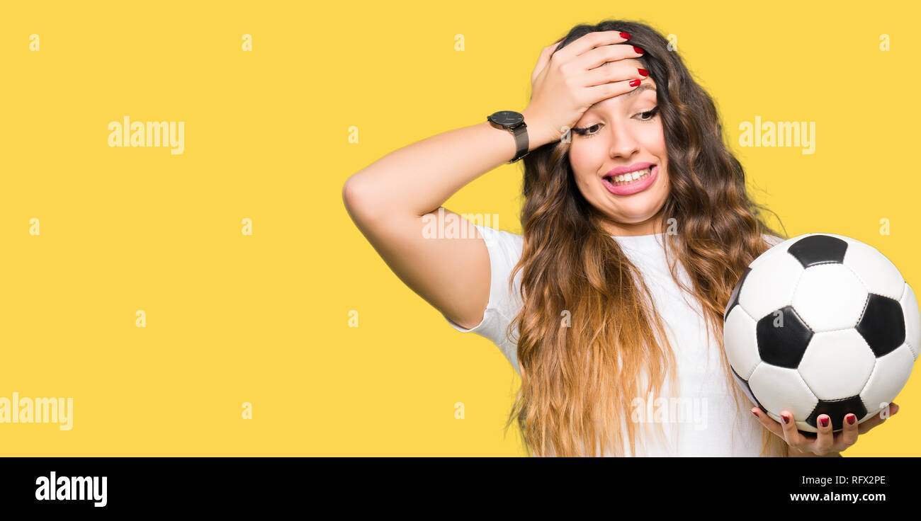 Young adult woman holding soccer football ball stressed with hand on ...