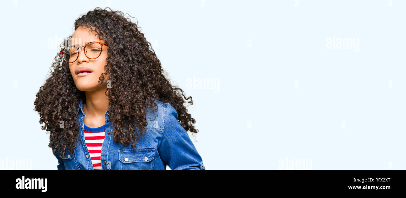 Young beautiful woman with curly hair wearing glasses with hand on ...