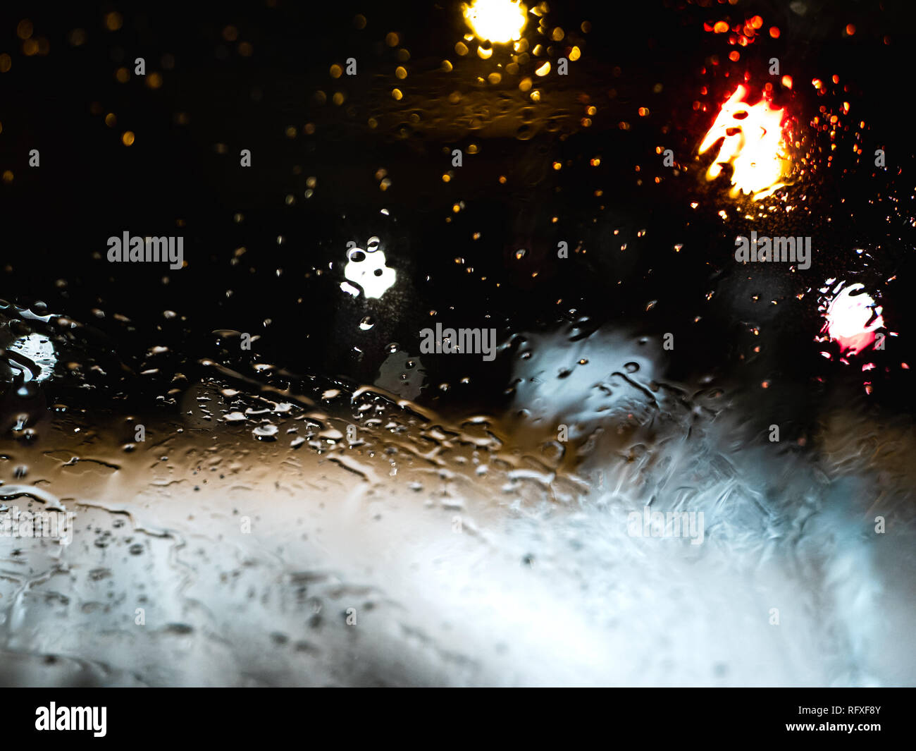 wet windshield with rain drops and street lights out of focus at night ...