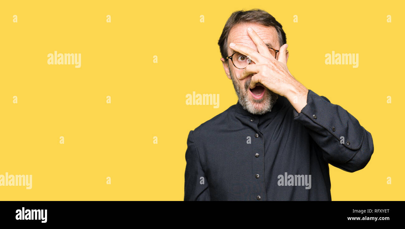 Middle age priest man wearing catholic robe peeking in shock covering ...
