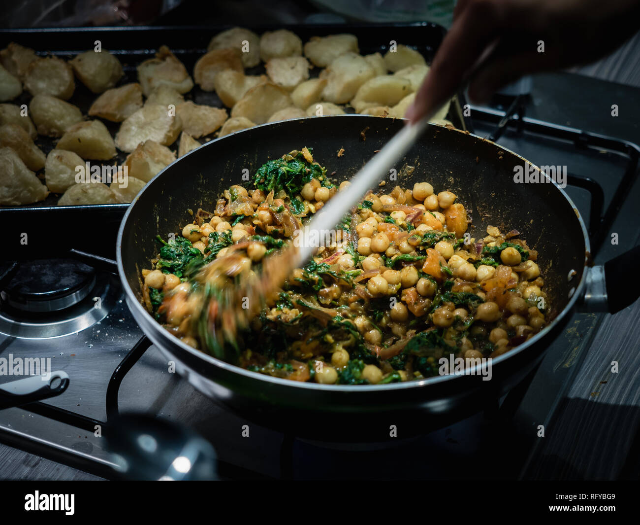 Hand stirring Indian chickpea and spinach curry in wok on gas stove ...