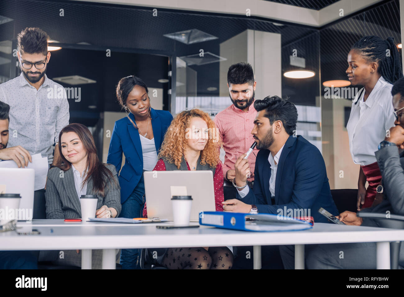 Young multi-ethnic work team exchanges ideas gathering around laptop ...