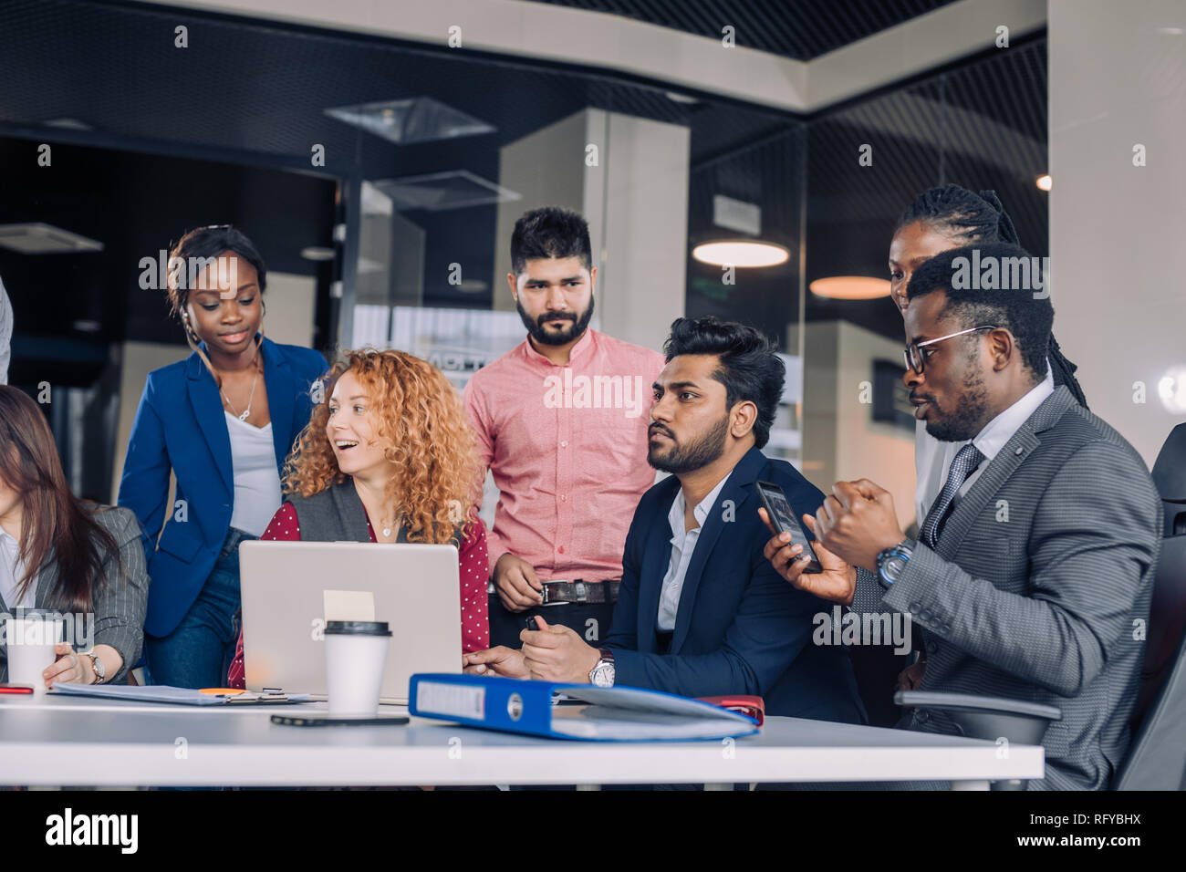Young multi-ethnic work team exchanges ideas gathering around laptop ...