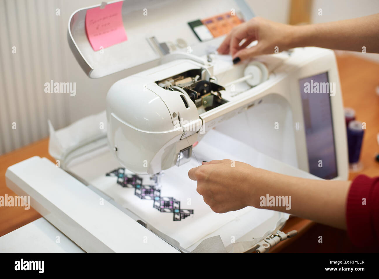 Close-up of woman hands filling thread in sewing machine on background ...