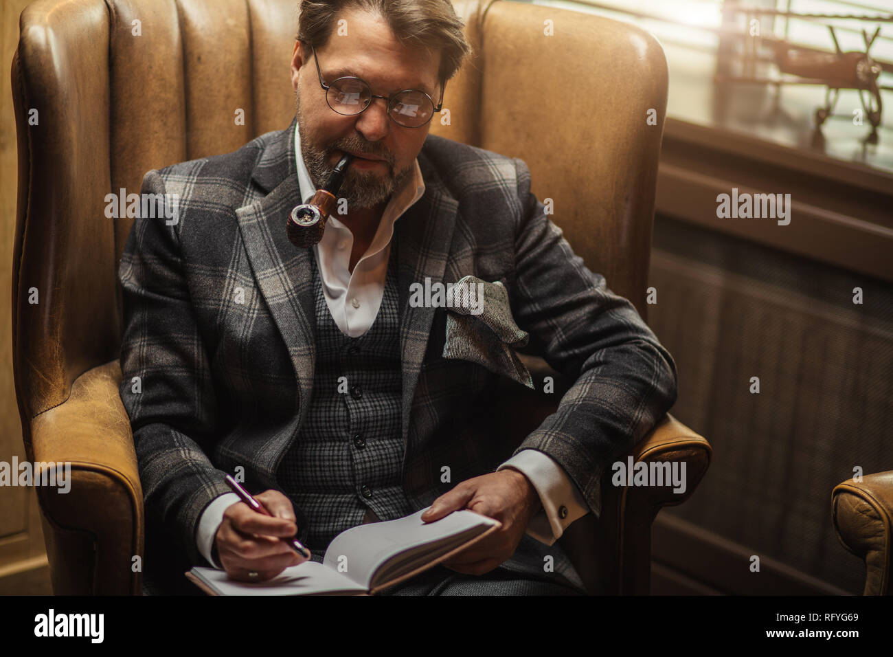 Mature businessman smoking tobacco pipe and making notes, working at ...