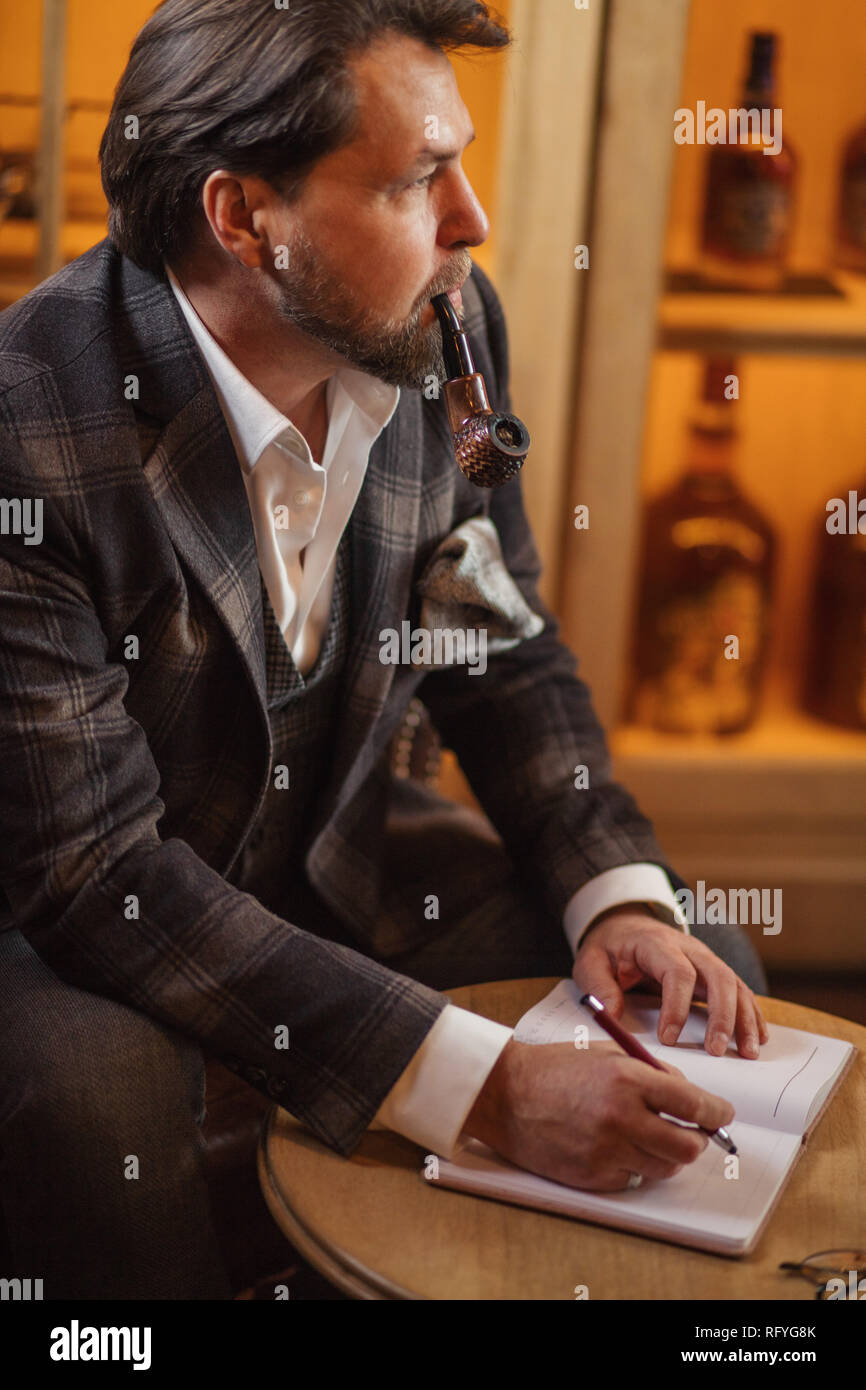 Mature businessman smoking tobacco pipe and making notes, working at ...