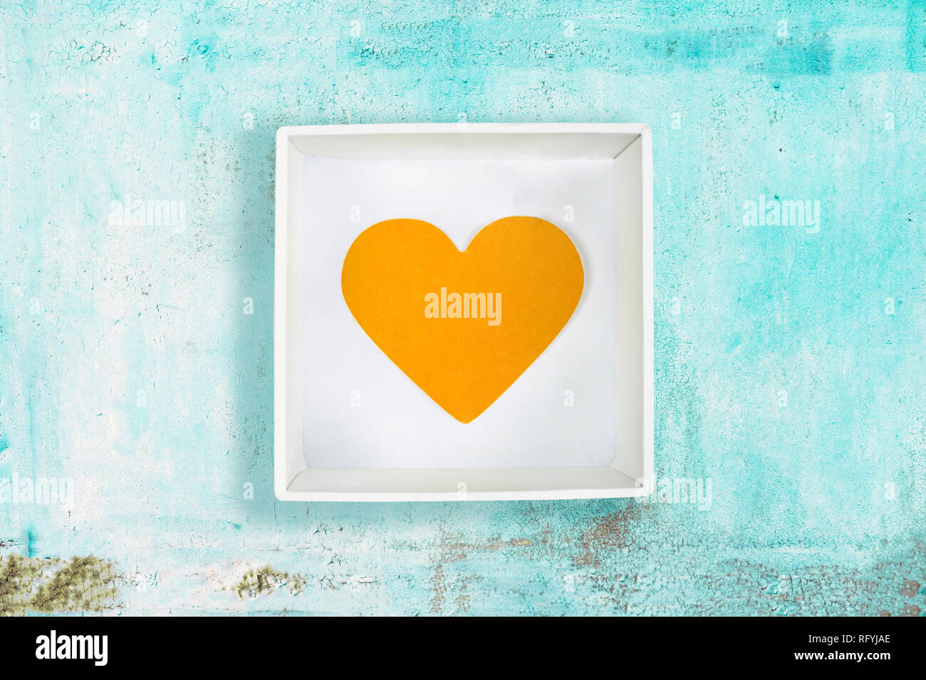 Yellow paper heart in white cardboard box on old turquoise metal ...
