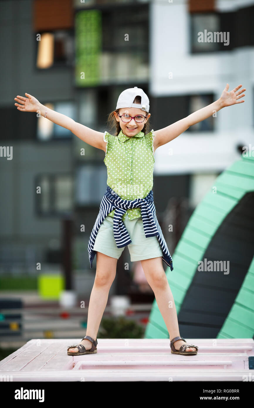 Girl in the playground. Happy child is standing with arms raised ...