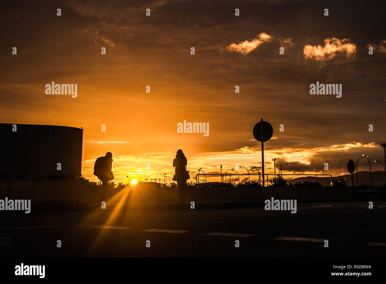 Two travelers watching a beautiful sunset from a city at a bus stop ...