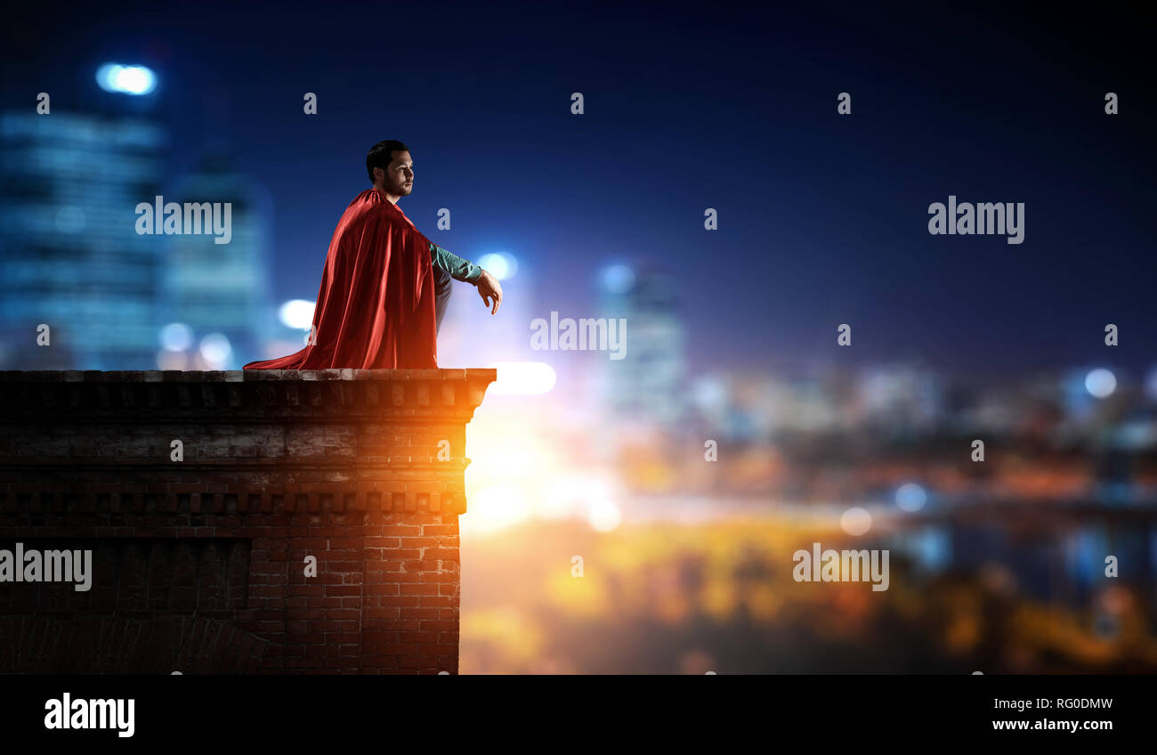 Thoughtful man in cape sitting on top of building. Mixed media Stock ...