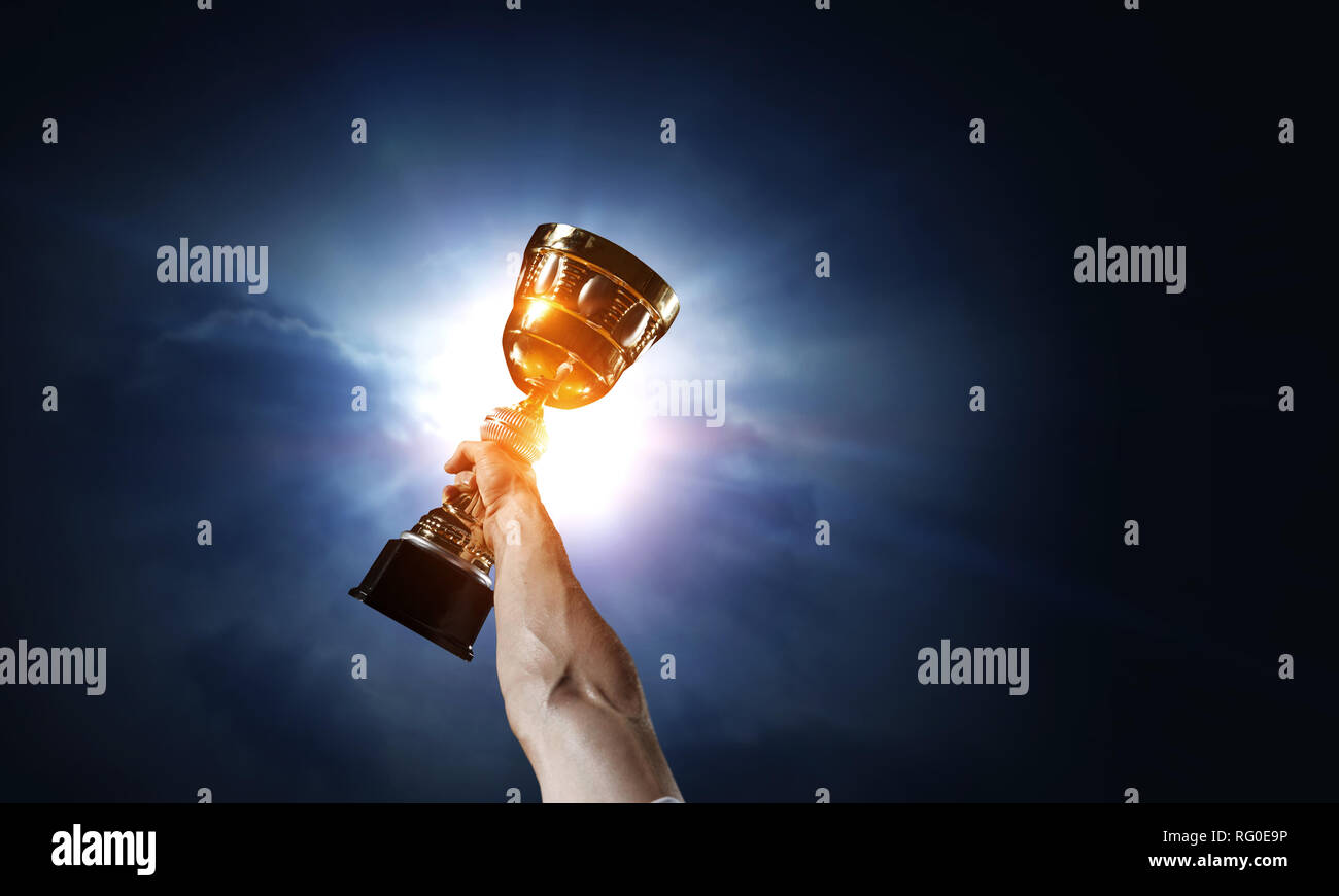 Hand of athlete holding cup trophy against stadium. Mixed media Stock ...