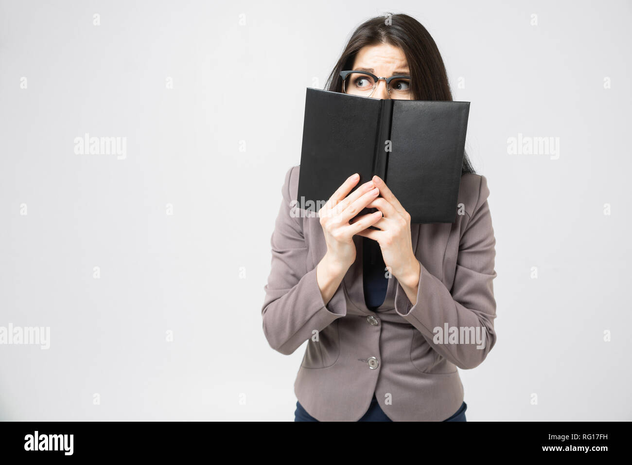 Young brunette covered the floor of her face with a diary isolated on a ...