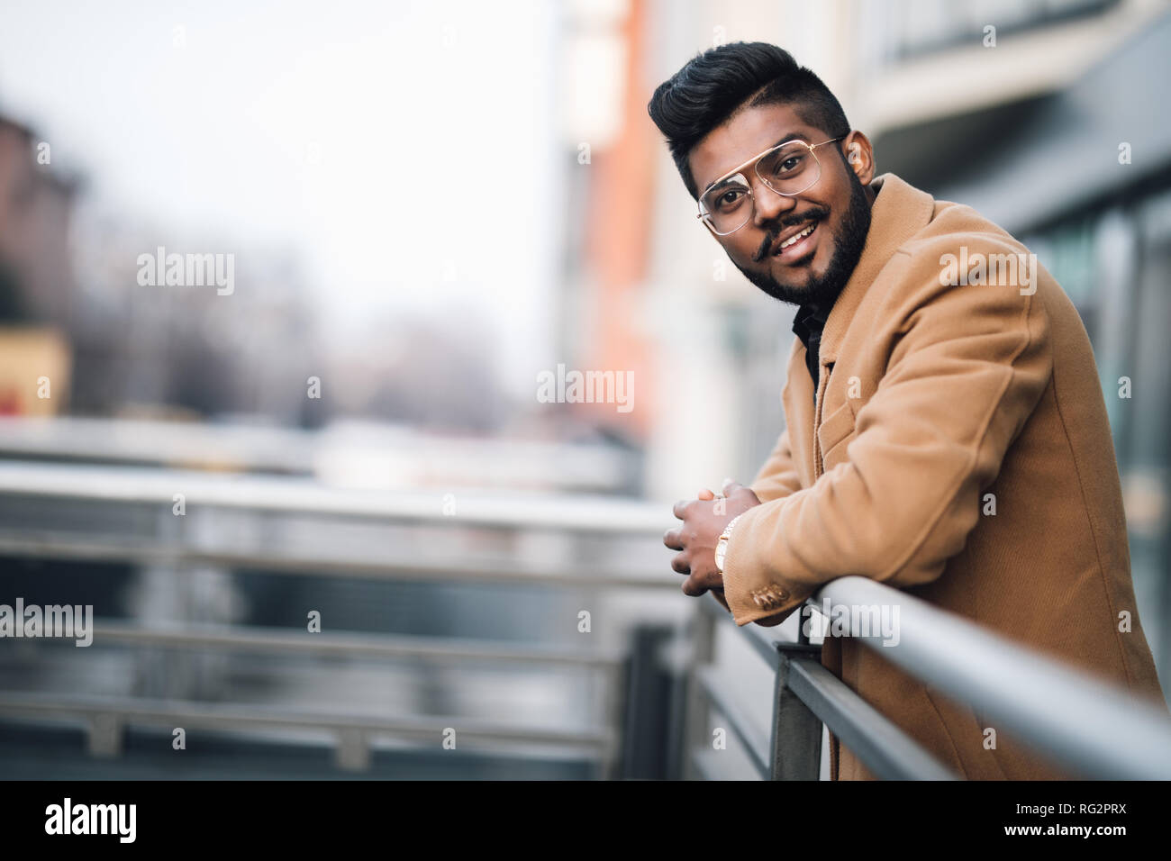 Young indian man standing outdoors with hands on handrail while ...