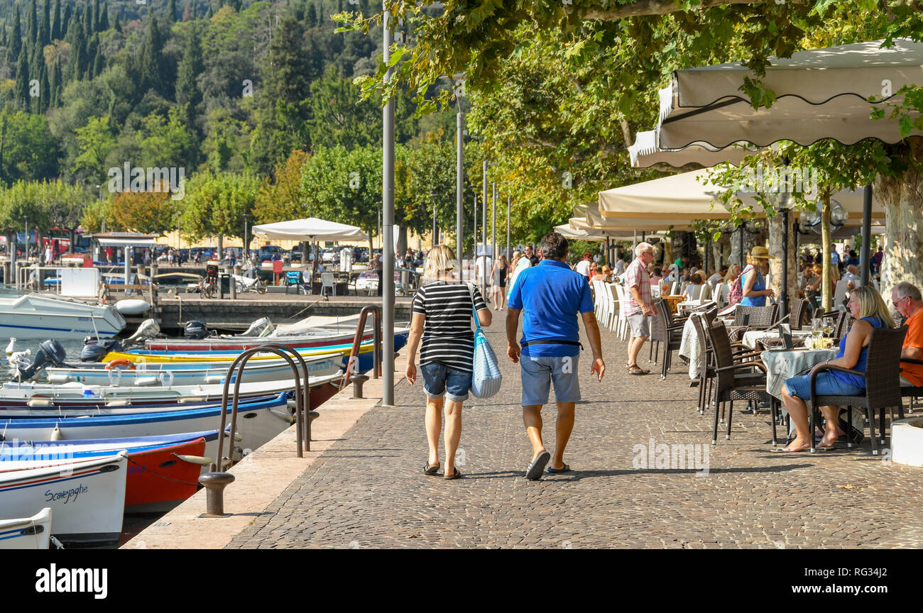 GARDA, ITALY - SEPTEMBER 2018: Two people walking along the promenade ...