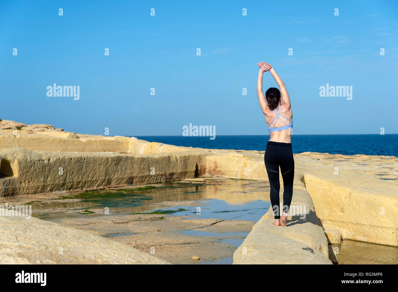 back view of a woman a doing a side body stretch outside by the sea ...