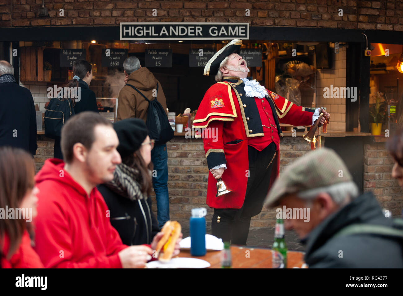 A town crier in uniform calls out the crowd at Camden Market in London ...