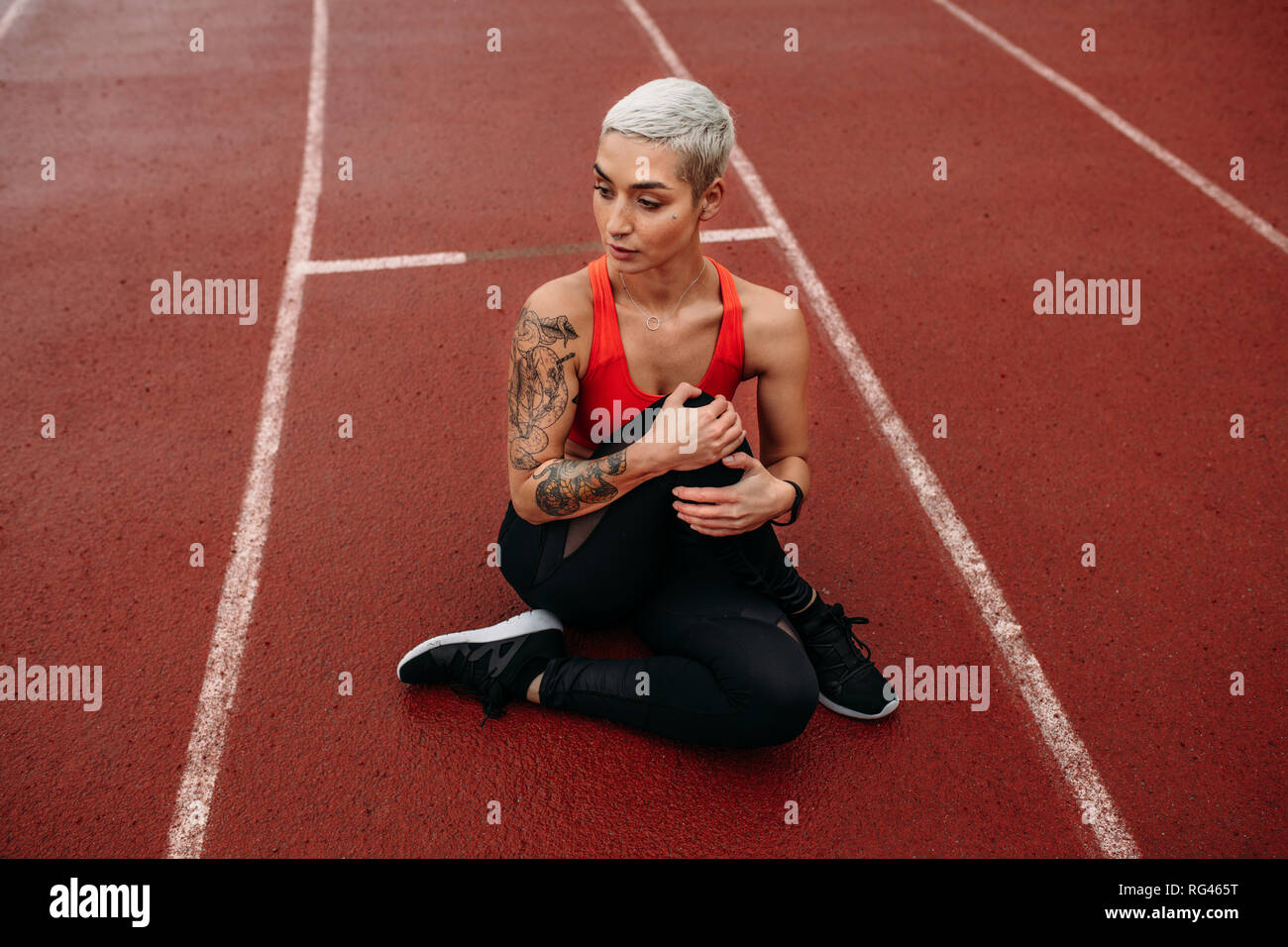 Female athlete doing stretching exercises sitting on running track ...