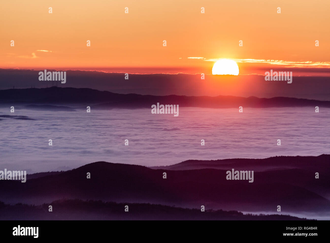 Beautiful sunset over a valley filled by fog with mountains and hills ...