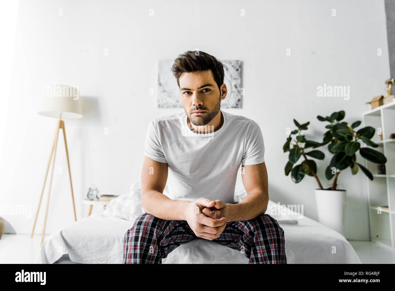 handsome serious man in pajamas sitting on bed at home Stock Photo - Alamy