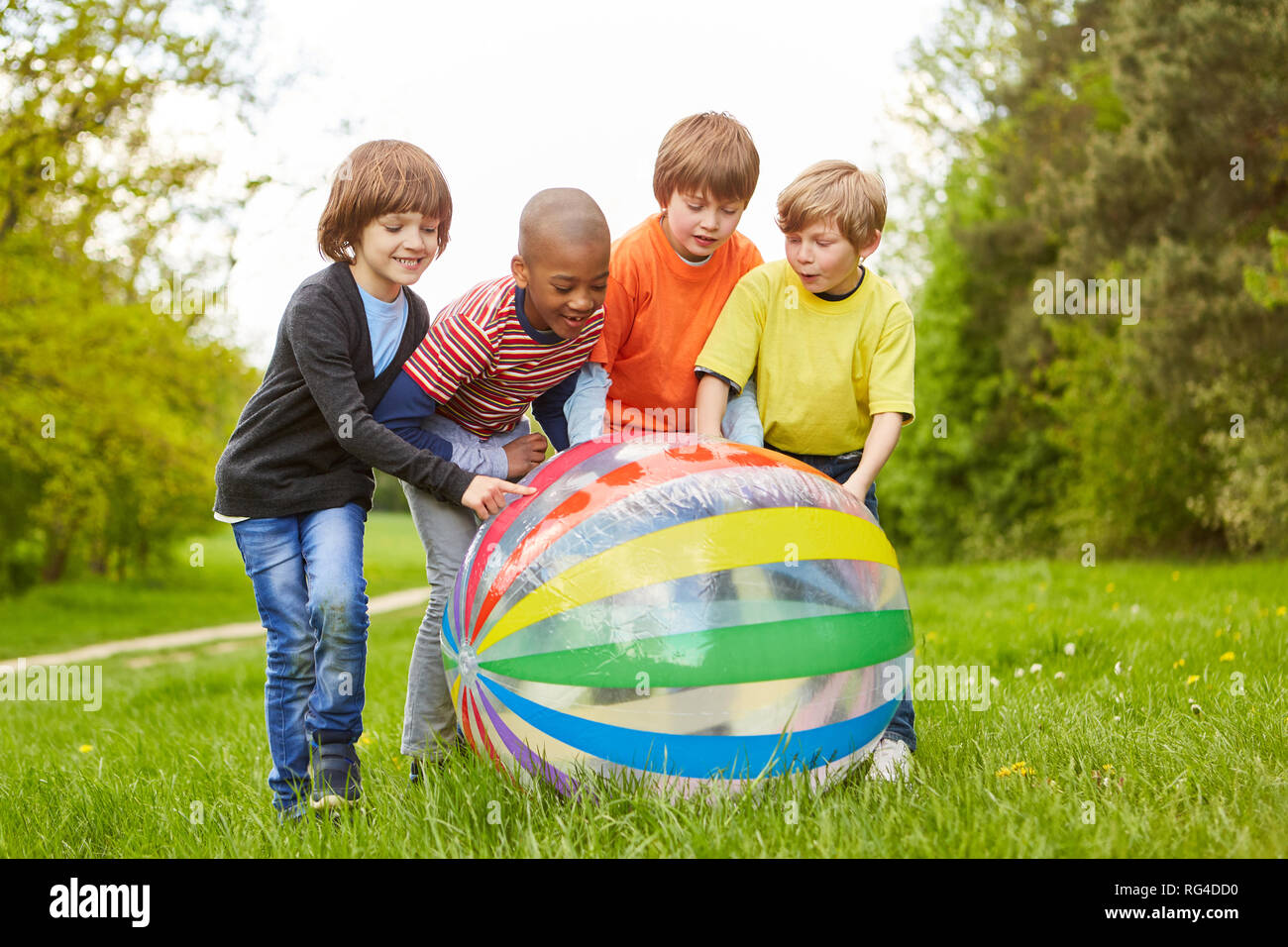 Group of kids as a team together rolls a ball in the park at a ...