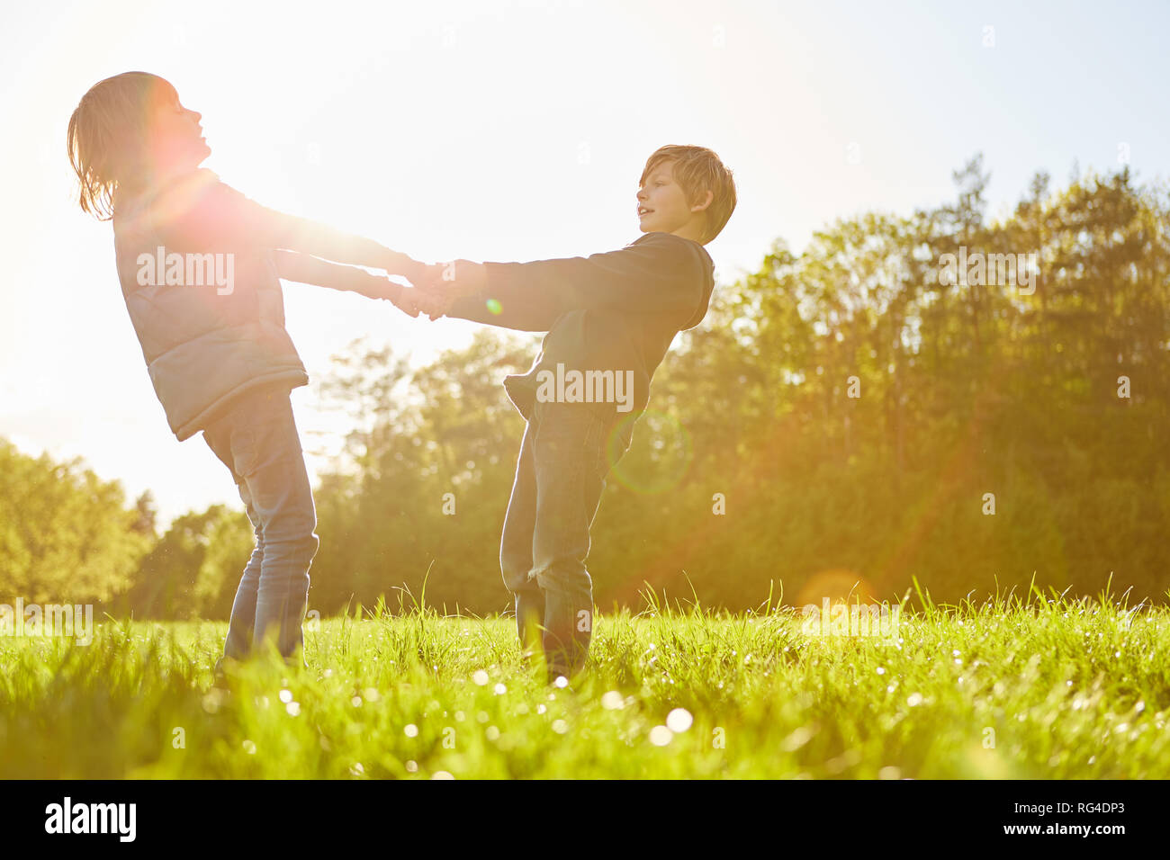 Two children are dancing on a meadow in the sunshine as a sign of ...