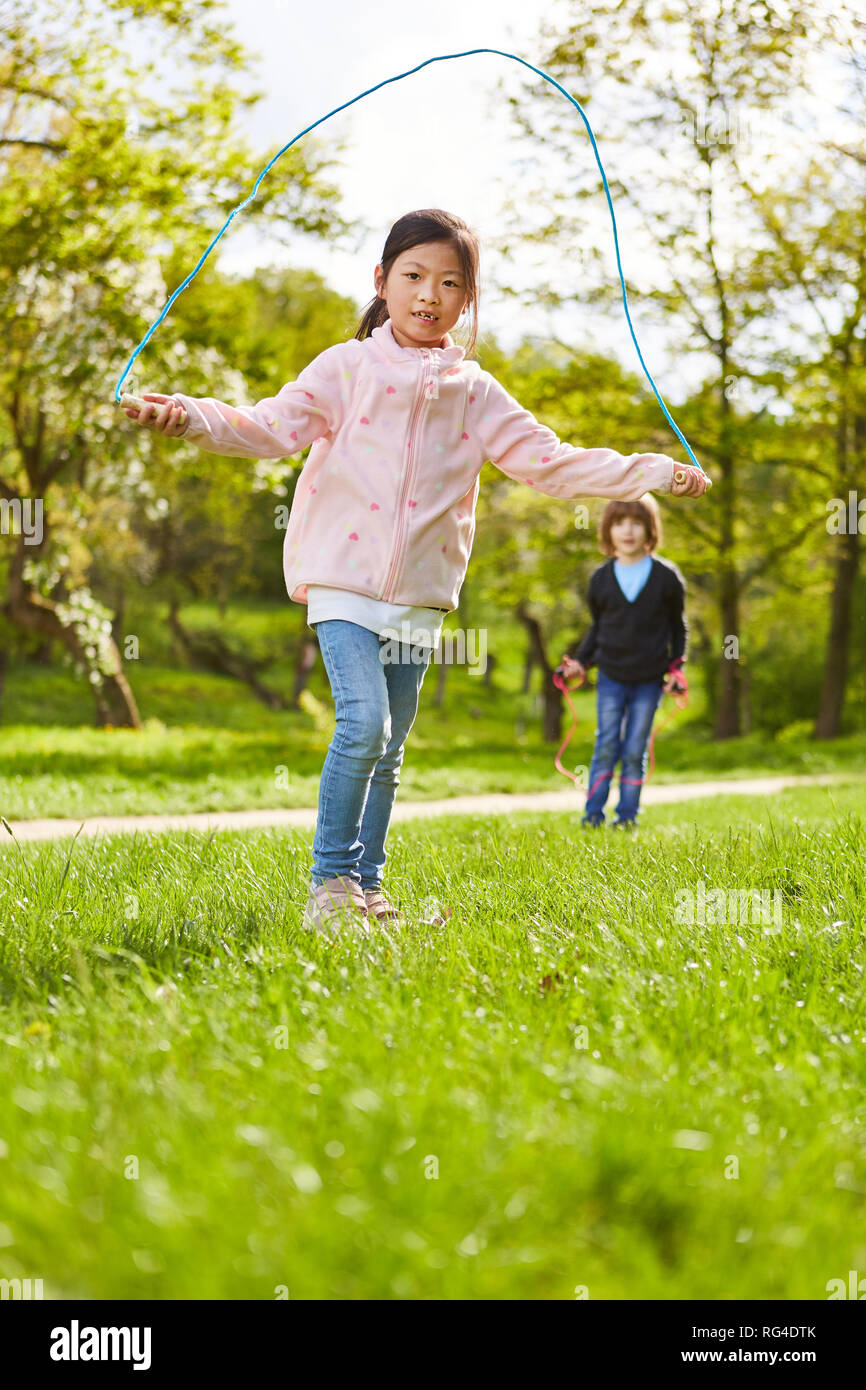Asian girl in jump rope on a meadow with girlfriend in the background ...