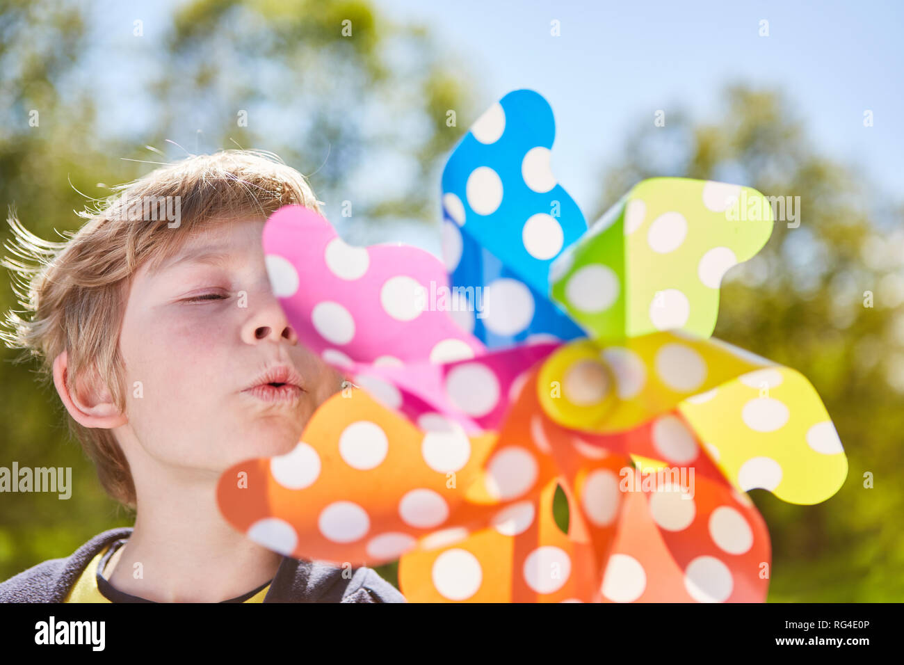 Little boy blows against a colorful windmill in summer at summer camp ...