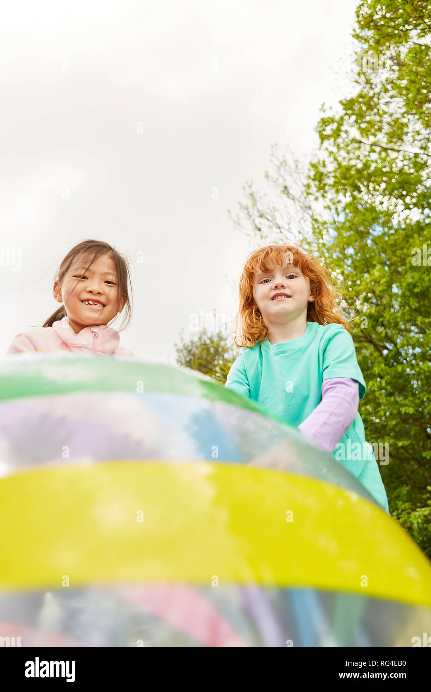 Two girls play together with a big ball in the park in summer Stock ...
