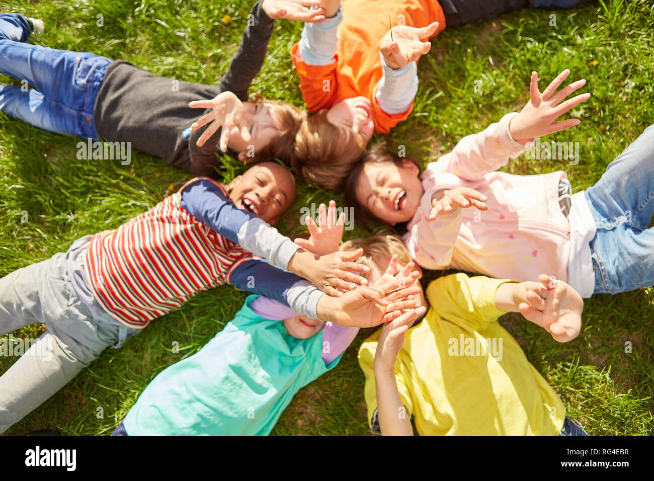 Group of laughing children lies in circle on a meadow as a sign of ...