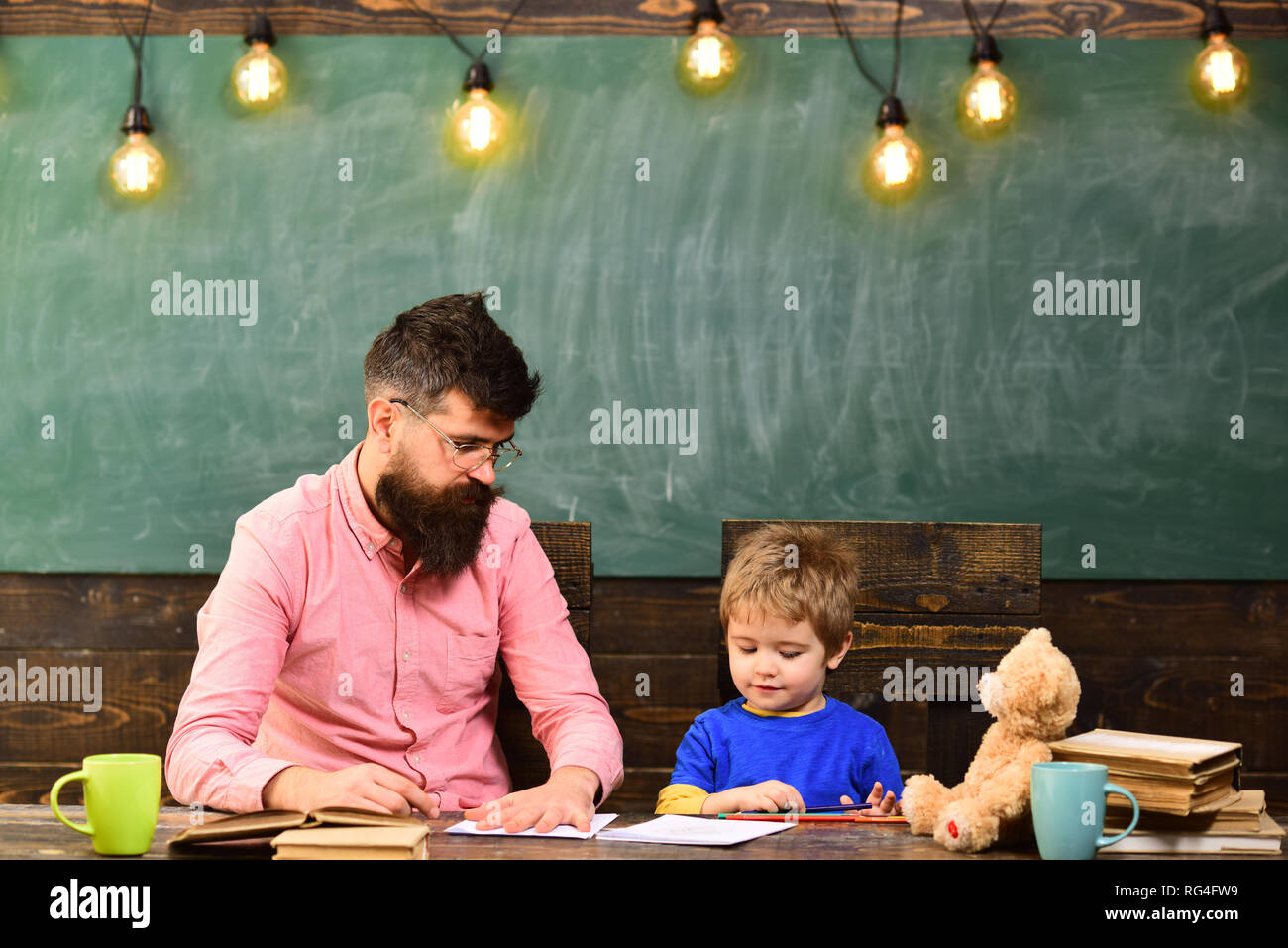 Teacher and small kid drawing together. Male teacher showing boy how to ...