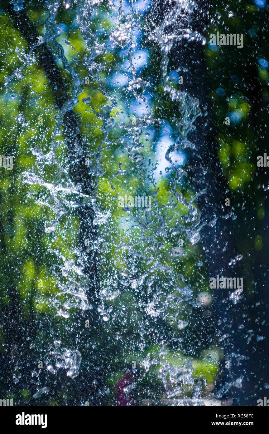 transparent falling water vertical flows against a blue sky and green ...