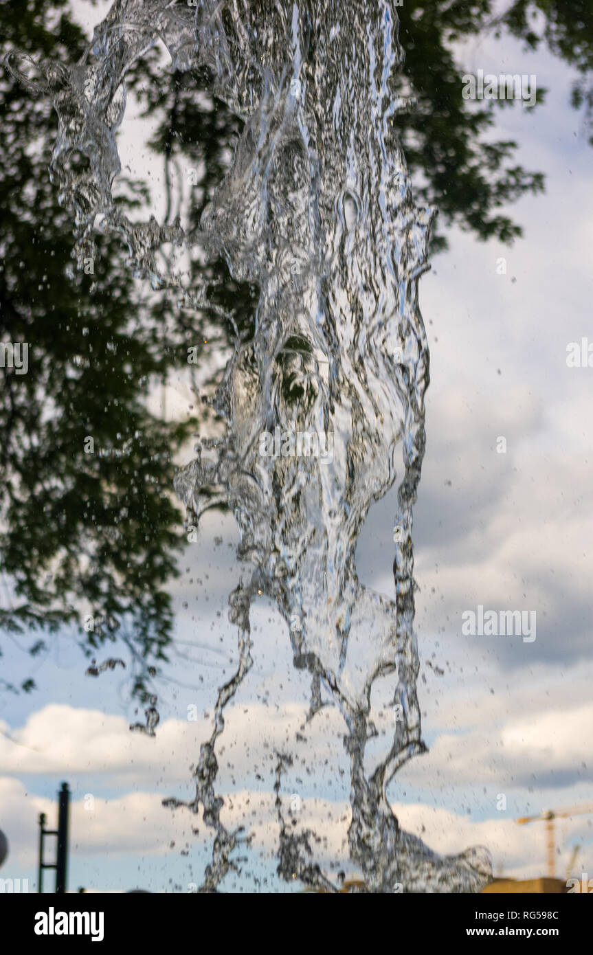 transparent falling water vertical flows against a blue sky and green ...