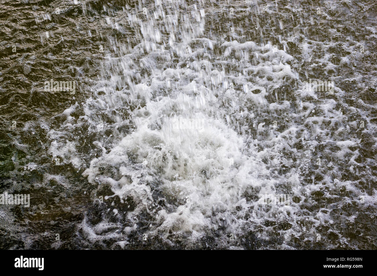 transparent falling water vertical flows against a blue sky and green ...