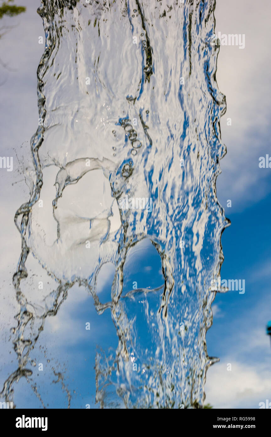transparent falling water vertical flows against a blue sky and green ...